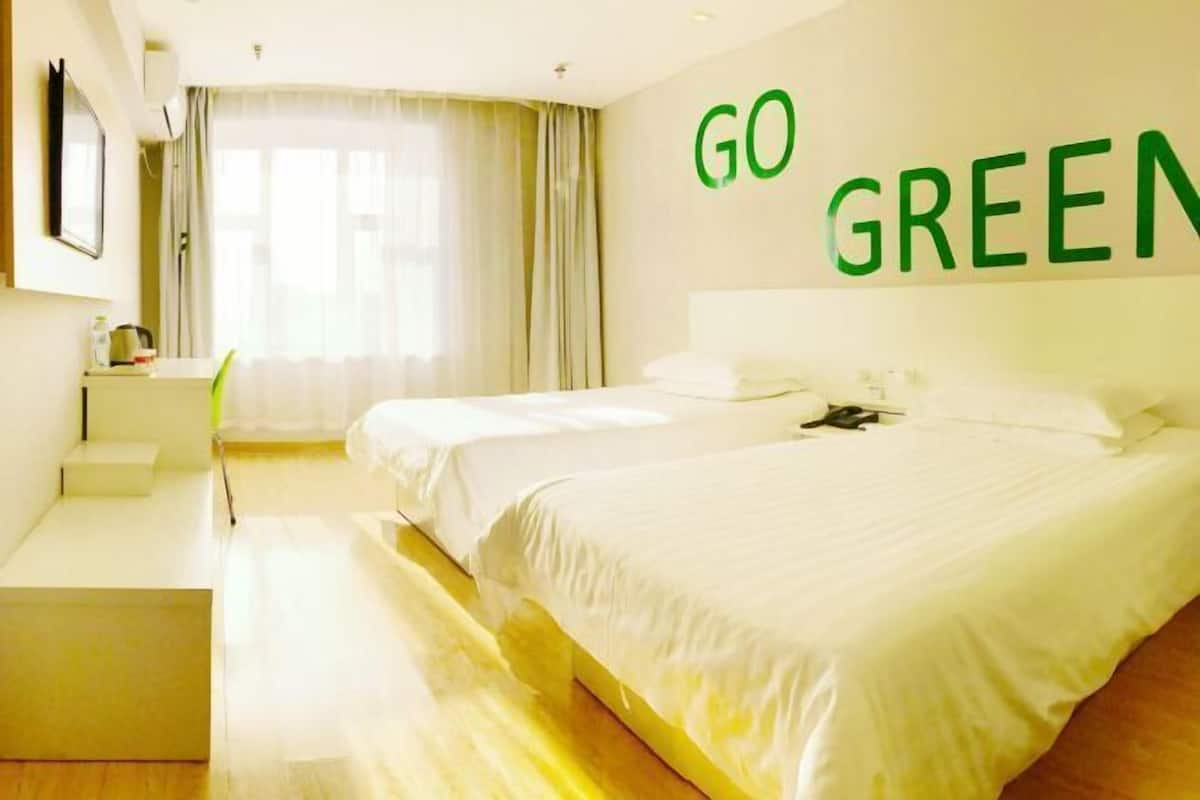 Quarto de hotel com cama, escrivaninha, cadeira e parede com a inscrição 'GO GREEN'.