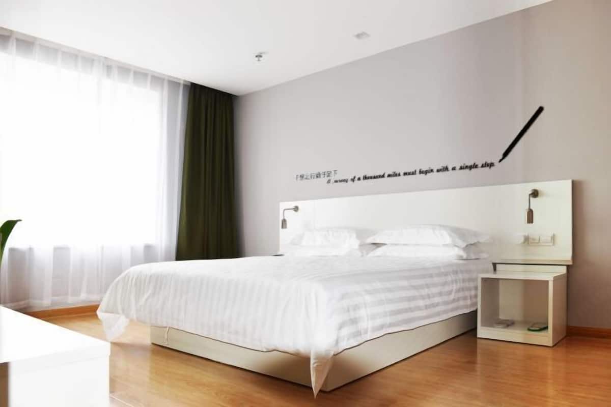 Quarto moderno com uma cama grande, mesa de cabeceira e luminária na parede.