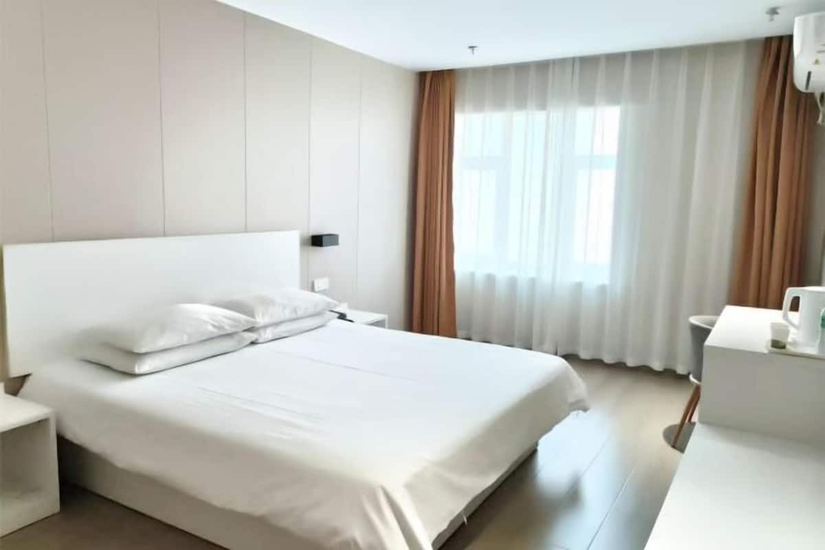 Quarto de hotel com uma cama grande, uma mesa de cabeceira, cortinas em uma janela e um ar condicionado fixado na parede.