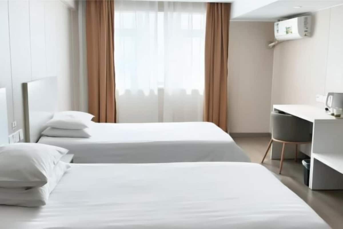 Quarto de hotel com duas camas, uma escrivaninha, uma cadeira e uma janela com cortinas.