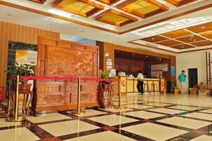 Um hall de hotel com balcão de recepção, um painel de madeira com obras de arte e um balcão de check-in.