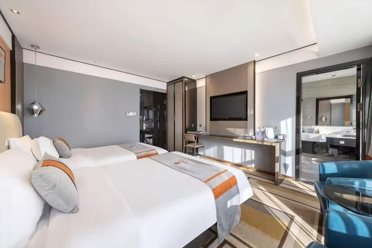 Quarto de hotel com duas camas, uma mesa, televisão e banheiro.