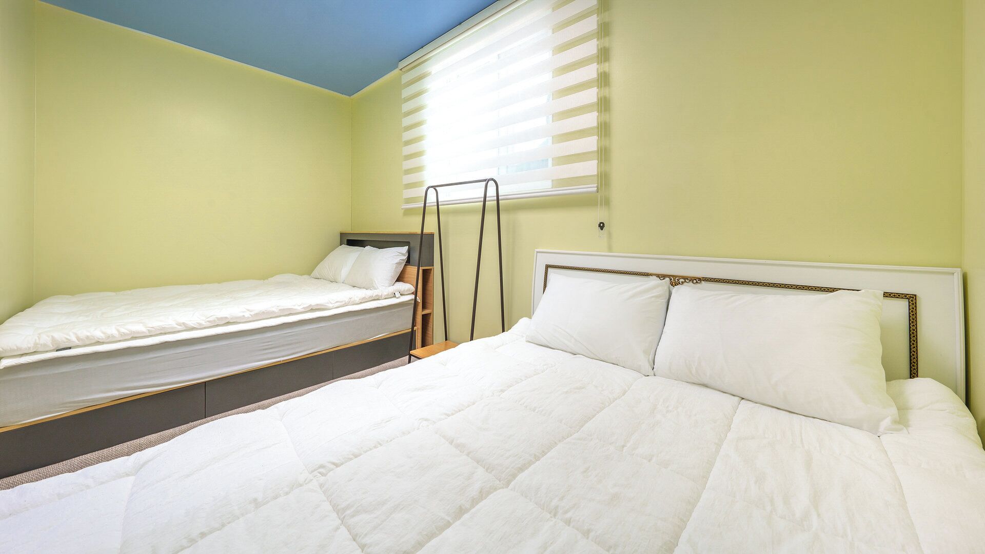 Quarto com duas camas, uma maior e outra menor, com janela e cortinas.