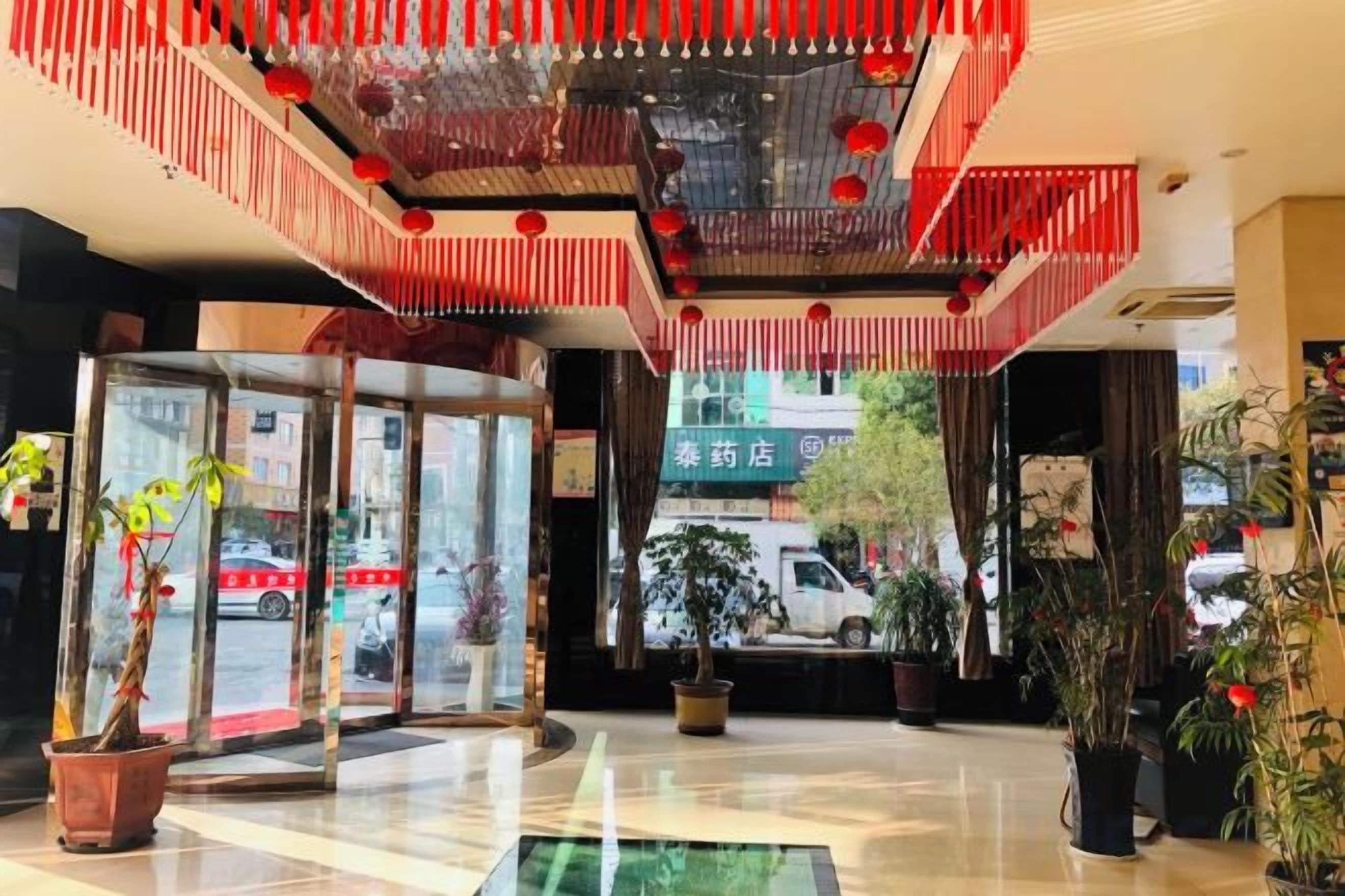Um hall de hotel com entrada de vidro, plantas em vasos e teto decorativo vermelho.