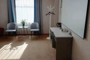 Quarto com escrivaninha, duas cadeiras, uma mesinha com planta e um cabideiro.