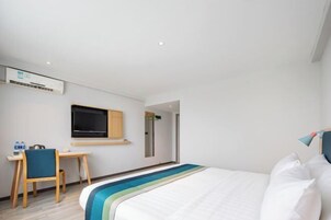 Quarto de hotel com cama, escrivaninha, cadeira, televisão e ar condicionado.