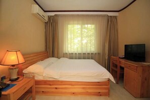 Quarto de hotel com cama de madeira, escrivaninha com televisão e janela com cortinas.