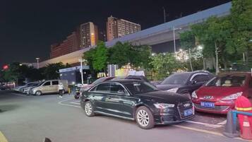 Um estacionamento com vários carros, uma faixa de pedestres e um edifício com sinalização iluminada ao fundo.