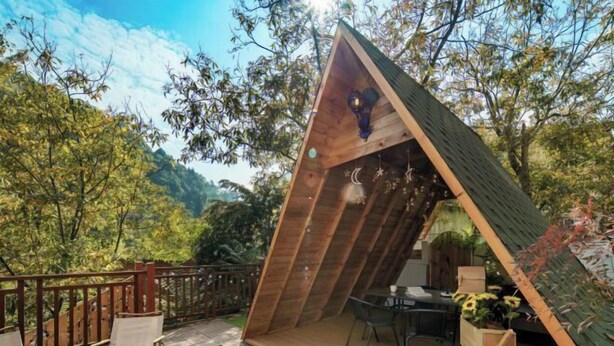 Estrutura triangular de madeira com deck, assentos e uma mesa com um vaso de girassóis.