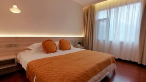 Quarto de hotel moderno com uma cama grande, uma mesa de cabeceira e uma janela com cortinas.