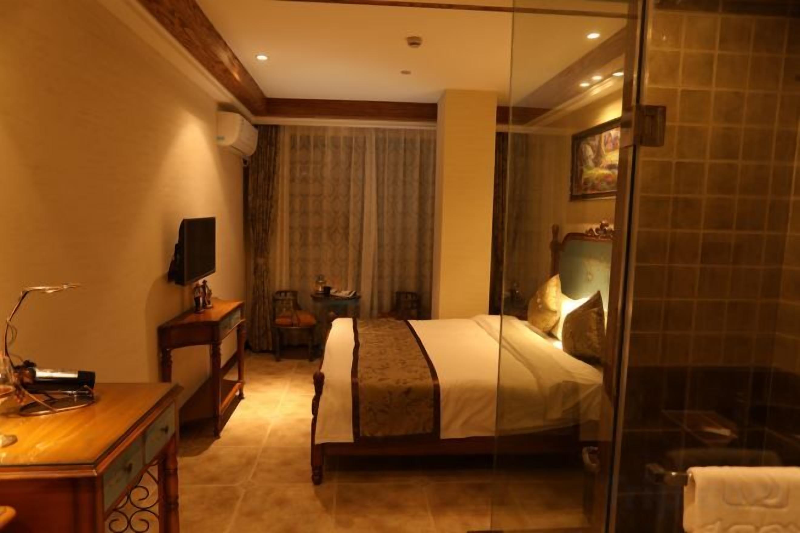 Quarto de hotel com cama, mesa de cabeceira, luminária e espelho.
