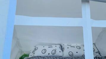 Quarto branco com cama, roupa de cama xadrez e travesseiros com carinhas sorridentes.