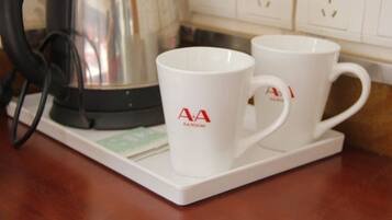 Duas canecas brancas com o logotipo 'AA ROOM' sobre uma bandeja branca, colocadas numa superfície de madeira com uma máquina de café ao fundo.