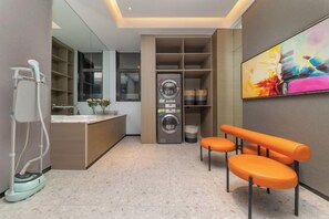 Quarto de hotel compacto com cozinha compacta, máquina de lavar, área de estar e uma pintura grande na parede.