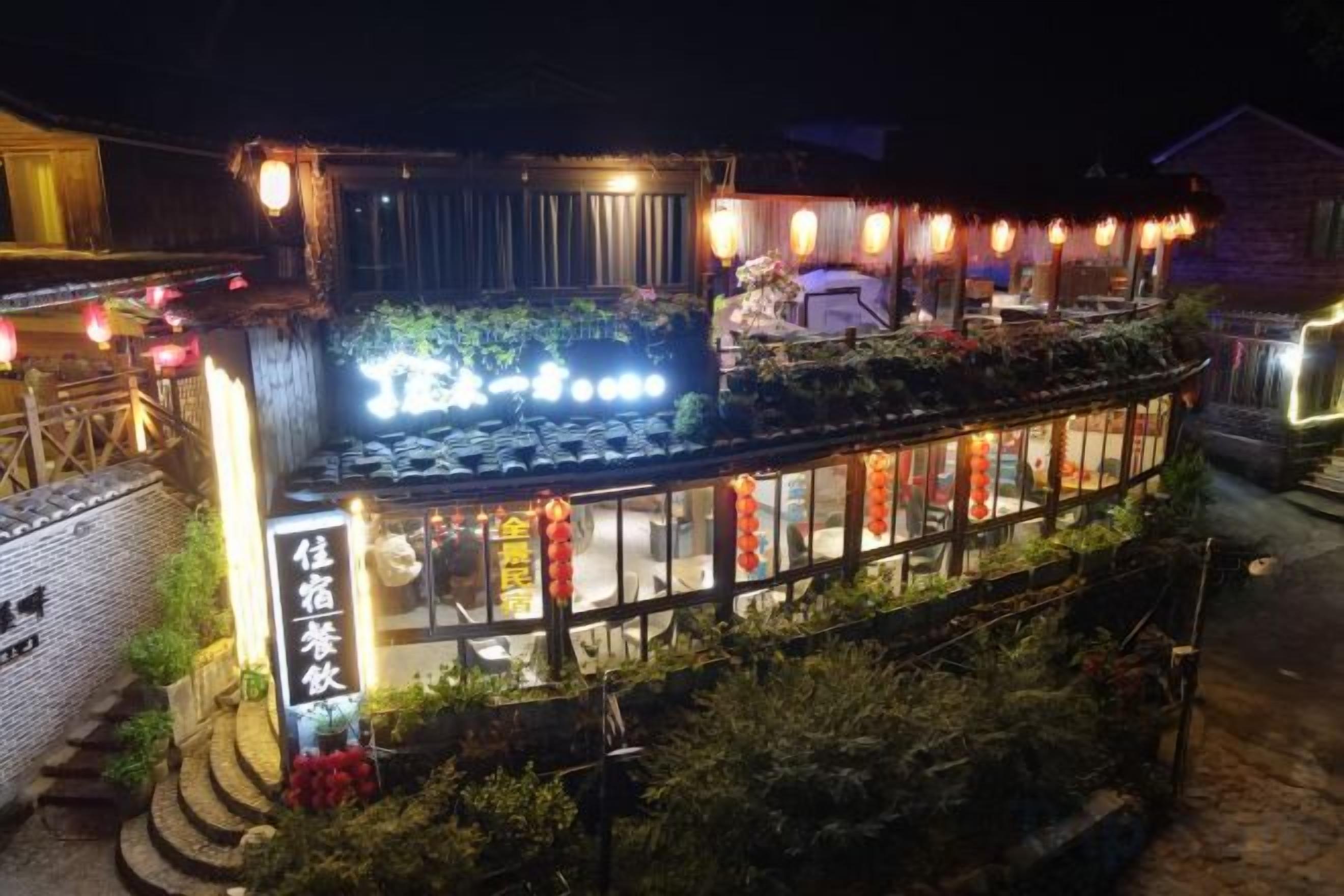 Restaurante com letreiro de neon, mesas ao ar livre e entrada visível.