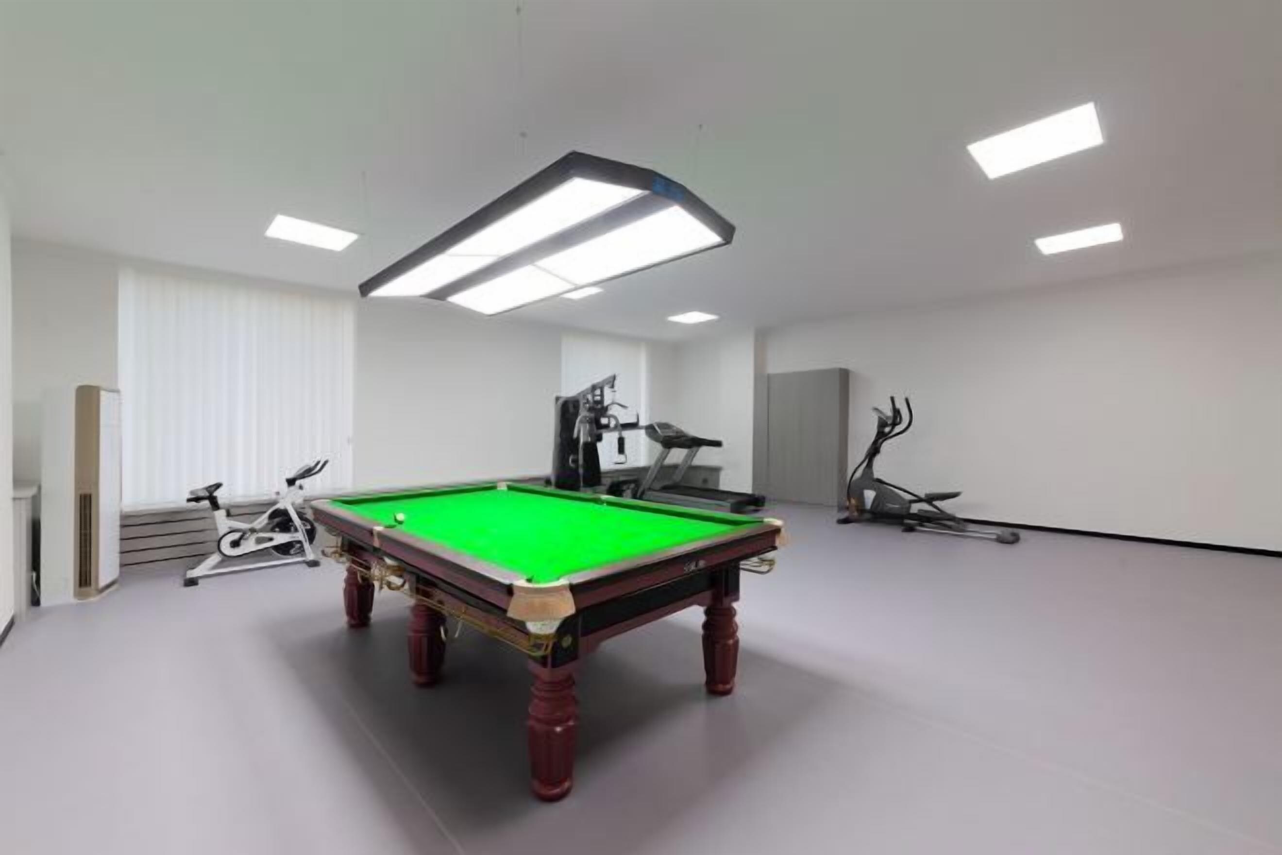Uma sala de bilhar com mesa de sinuca, bicicletas ergométricas e iluminação pendente.