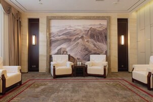 Quarto com um grande mural na parede, duas poltronas, uma pequena mesa e piso coberto por carpete.