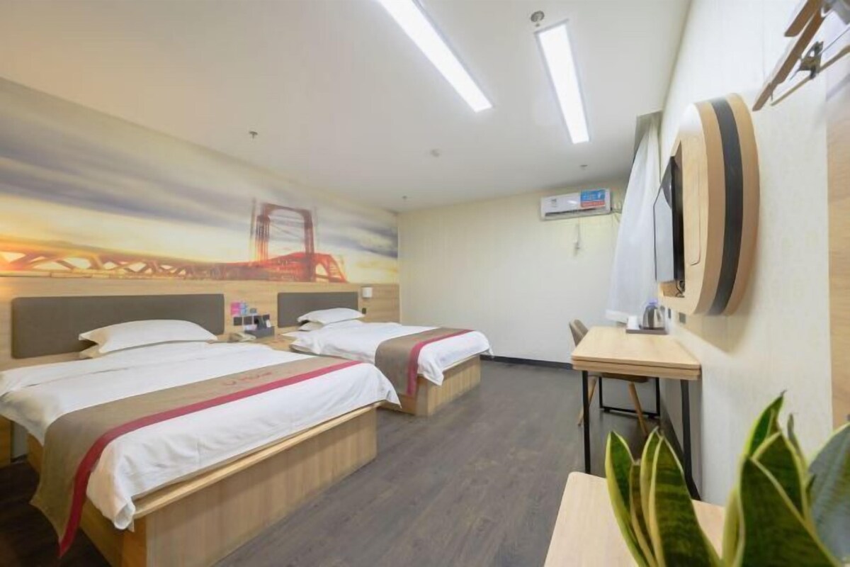 Quarto de hotel com duas camas, uma escrivaninha, uma cadeira, uma TV e ar condicionado fixado na parede.