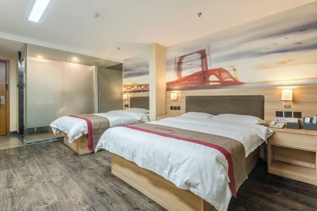 Quarto de hotel com duas camas, uma janela ampla e um quadro de uma ponte na parede.