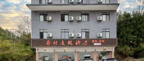 Um edifício de dois andares com várias unidades de ar condicionado, uma placa com caracteres chineses e diversos carros estacionados na frente.