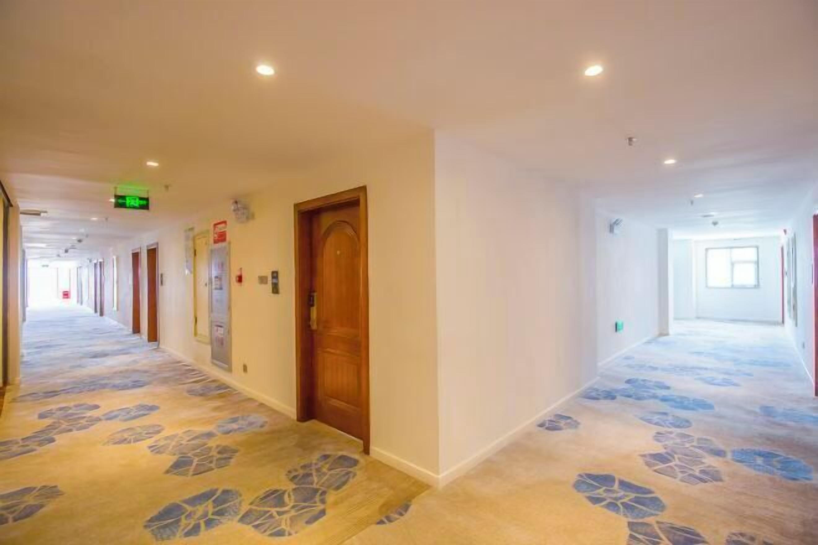 Corredor de hotel com carpete estampado, portas de madeira e iluminação embutida.