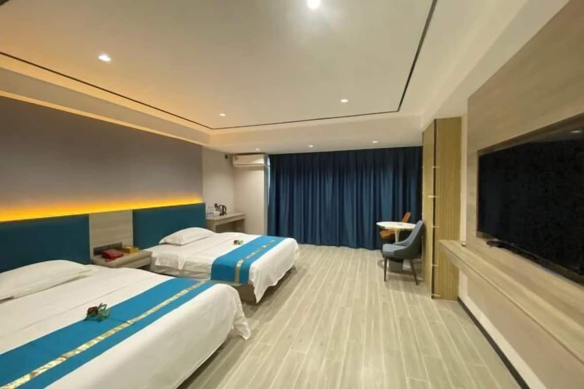 Quarto de hotel com duas camas, uma mesa, uma cadeira, uma TV e uma janela grande com cortinas.