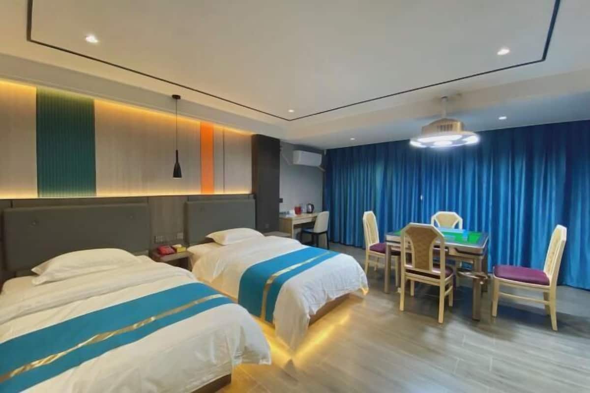 Quarto de hotel com duas camas, uma escrivaninha, cadeiras e uma janela grande com cortinas.