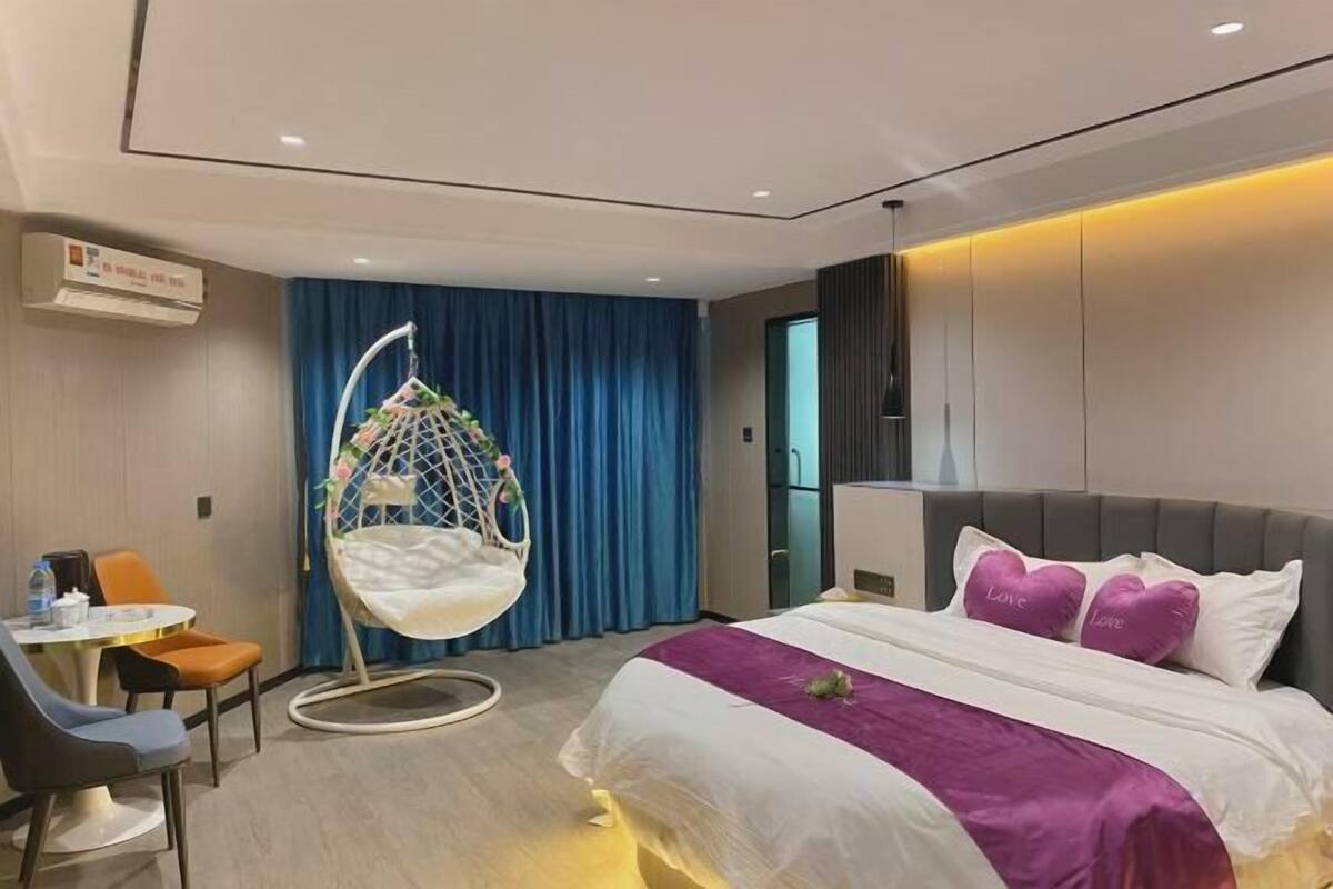 Quarto de hotel moderno com cama, cadeira suspensa, área de refeições e janela com cortinas.