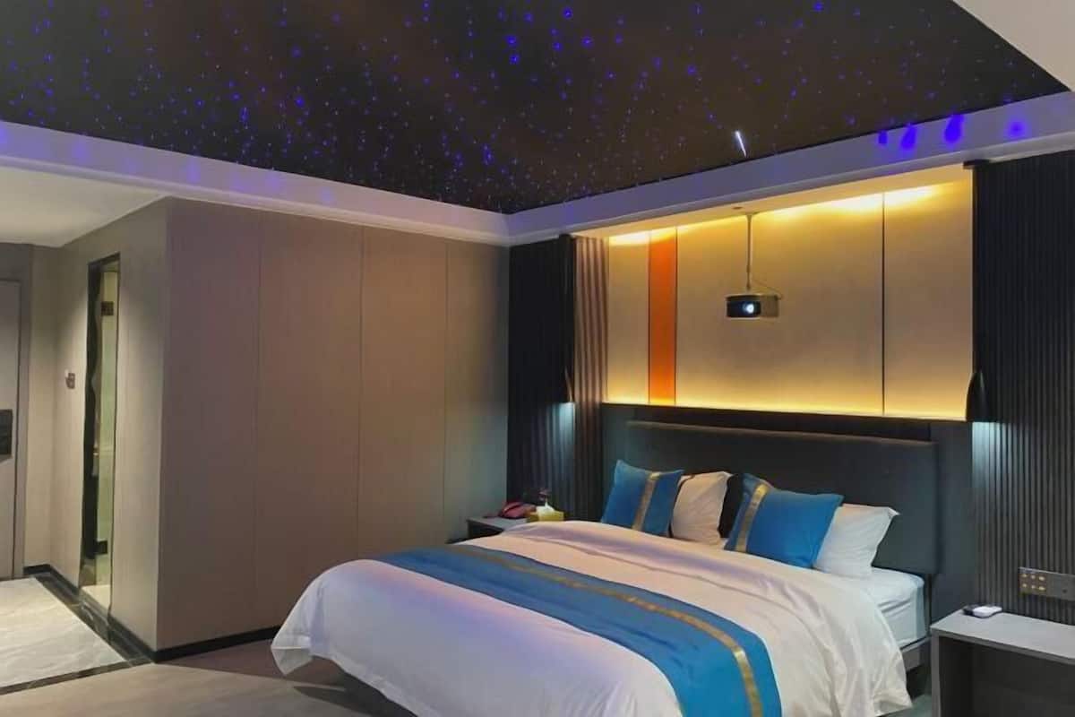 Quarto de hotel moderno com uma cama grande, teto com design de estrelas e projetor fixado na parede.