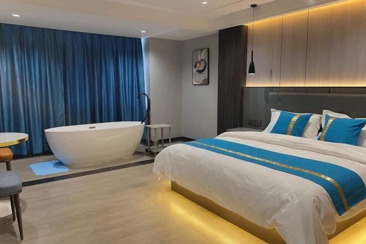 Quarto de hotel moderno com uma cama grande, uma banheira e uma pequena mesa.
