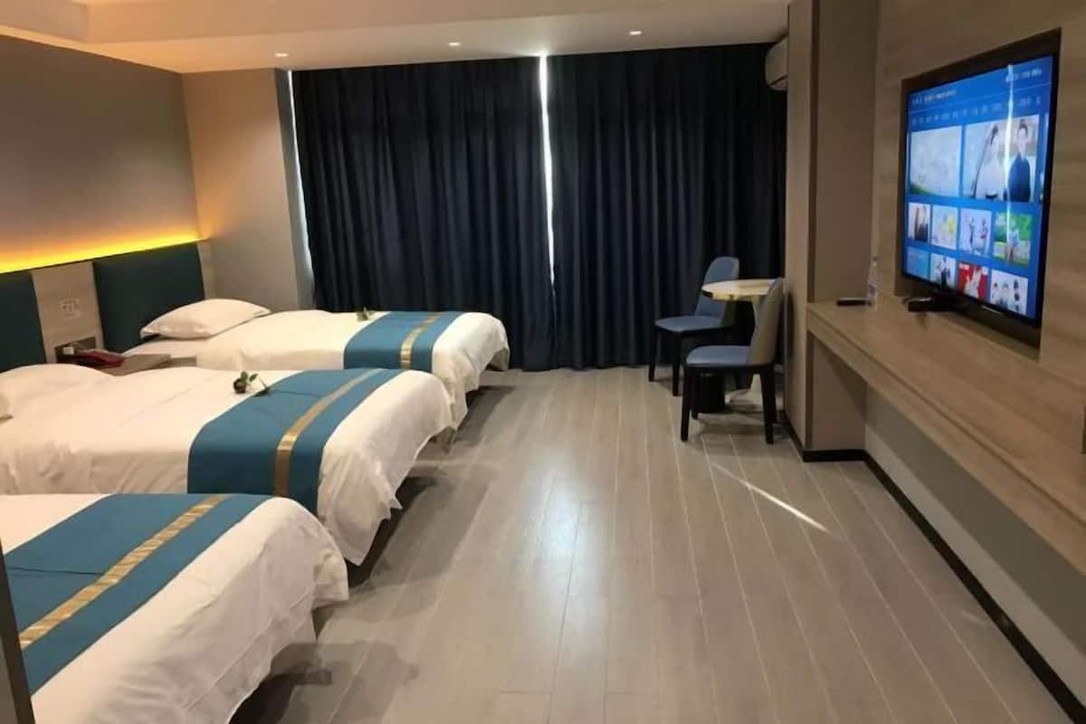 Quarto de hotel com duas camas, uma escrivaninha, uma cadeira, televisão e uma janela grande com cortinas.