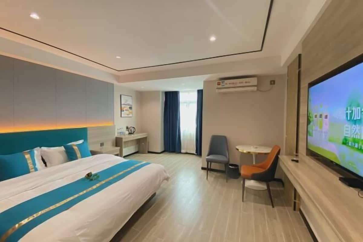 Quarto de hotel com cama, escrivaninha, cadeira, televisão e janela.