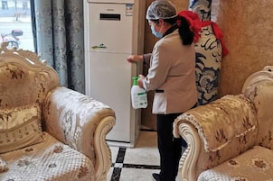 Uma pessoa em um quarto com móveis requintados, uma geladeira e parede com padrão.