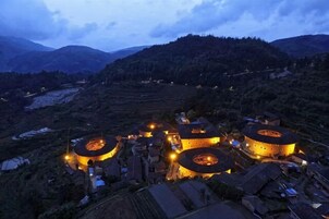 Uma vila rural com edifícios de telhados arredondados tradicionais, rodeada por montanhas e campos.