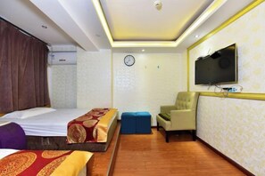 Quarto de hotel com cama, televisão, cadeira e escrivaninha.