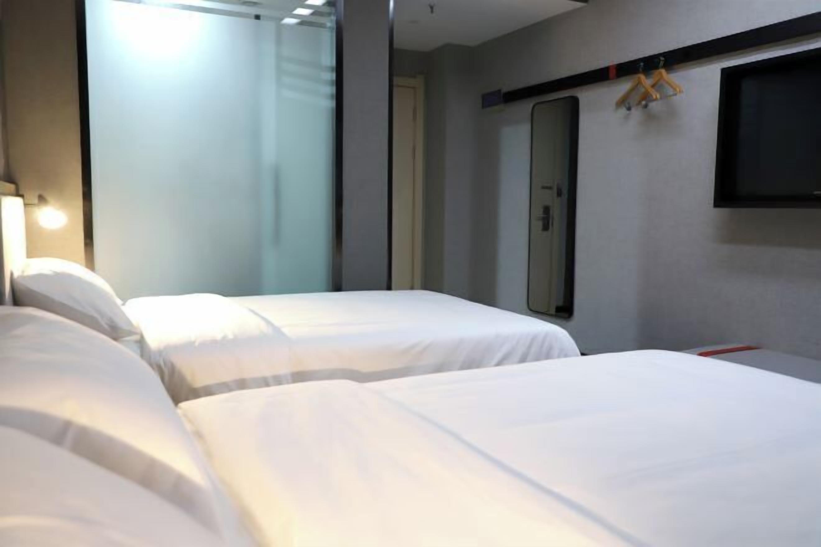 Quarto de hotel com duas camas, um espelho grande e uma televisão presa na parede.