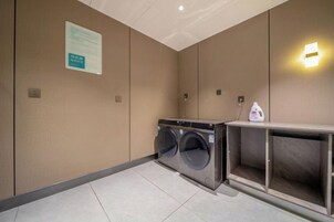 Quarto de hotel com máquina de lavar, armário e luminária fixada na parede.