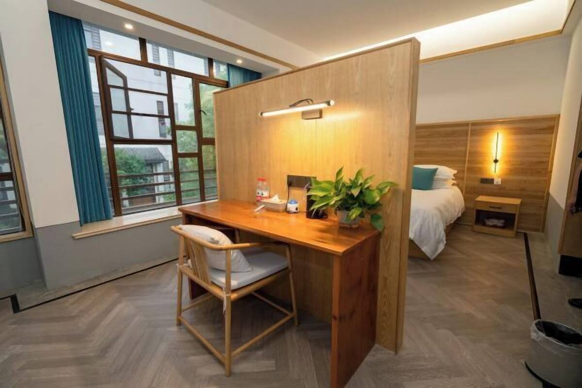 Quarto moderno com escrivaninha de madeira, cadeira, mesa de cabeceira e cama com colcha branca.