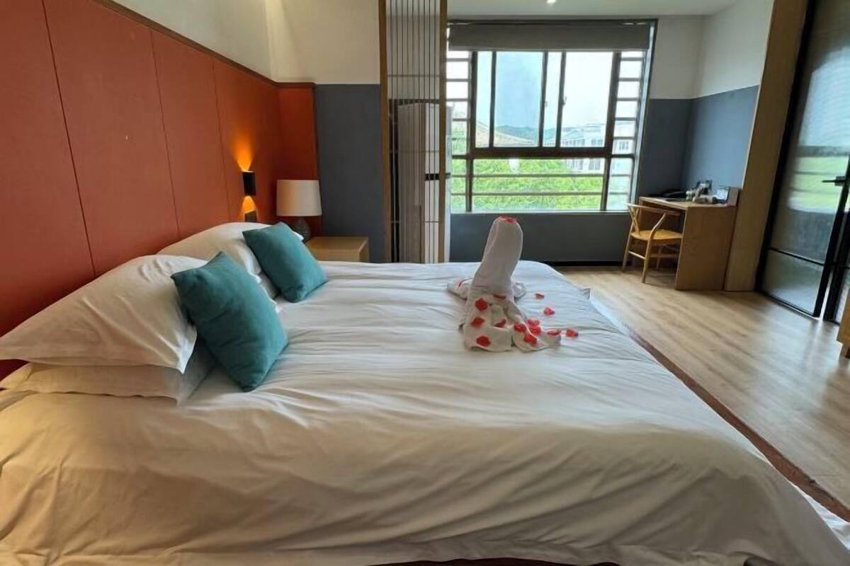 Quarto de hotel com uma cama grande, uma escrivaninha e vista para áreas verdes.
