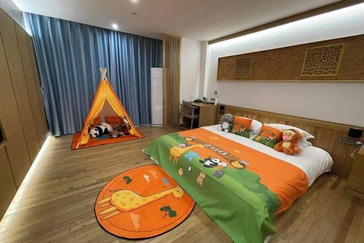 Quarto de hotel com cama, uma tenda infantil, tapete redondo e parede com painéis decorativos.