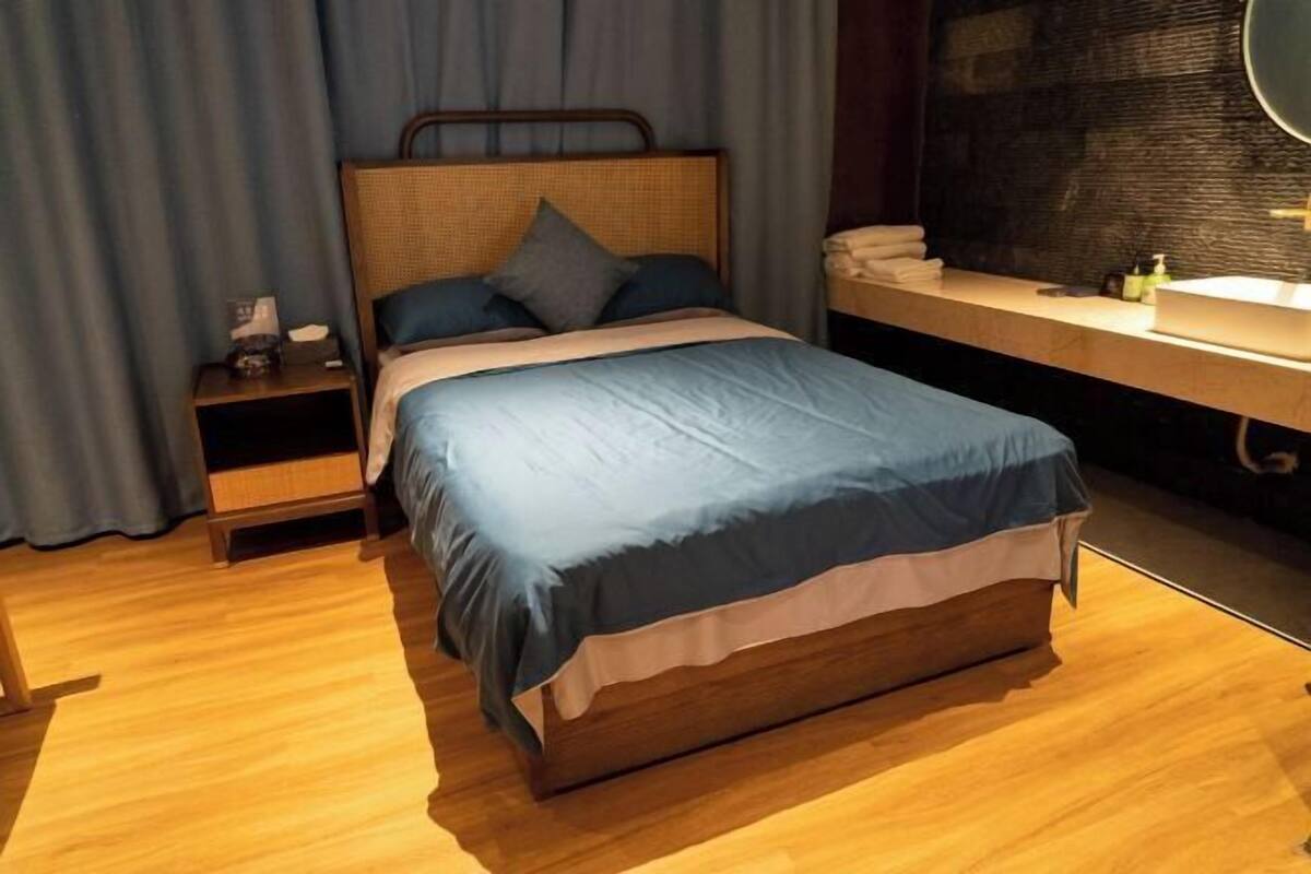 Uma cama bem arrumada com cabeceira de madeira, mesa de cabeceira com abajur e um espelho grande na parede.