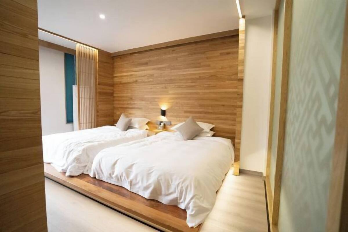 Quarto de hotel moderno com parede de madeira, duas camas, uma mesa de cabeceira e um abajur.