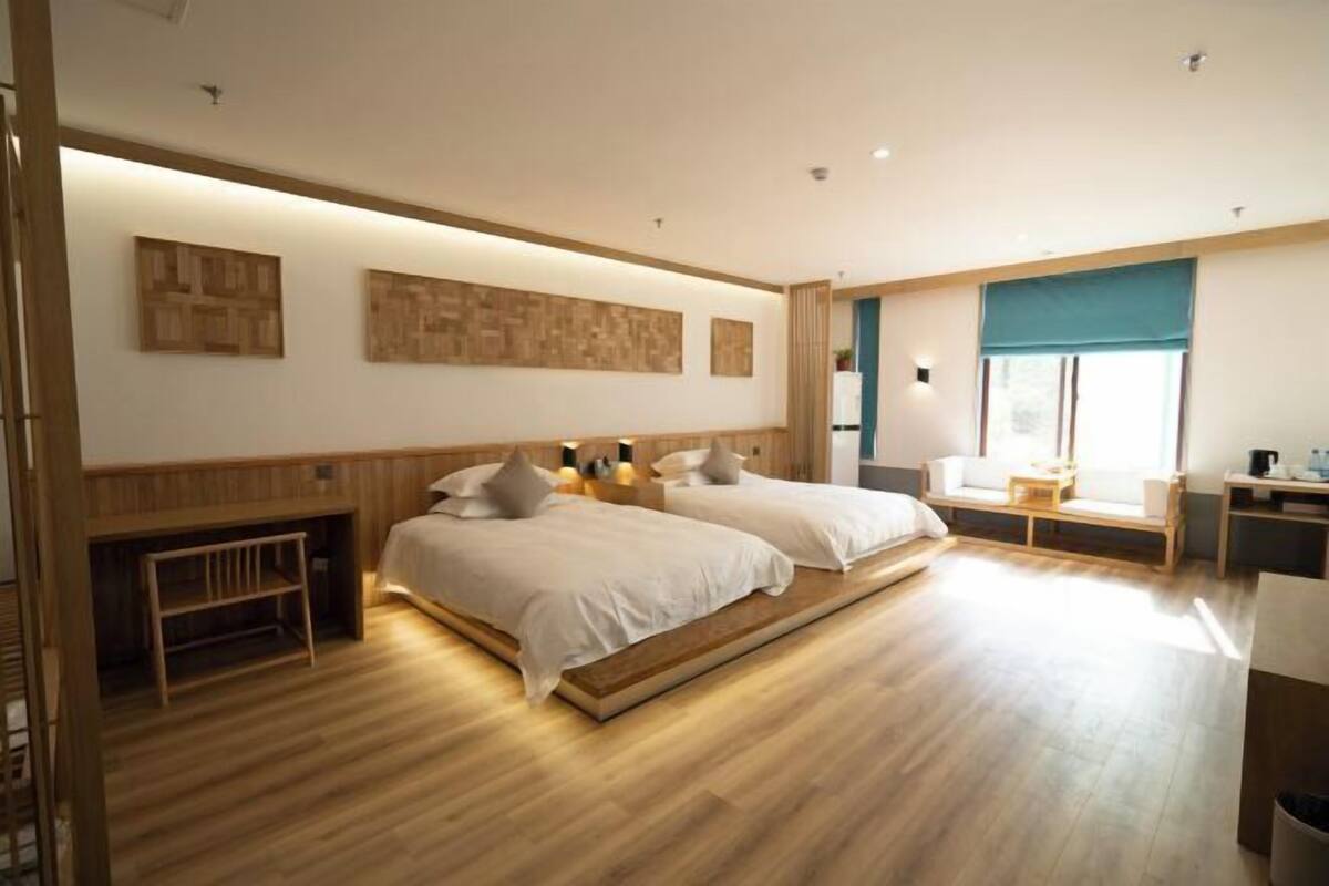 Um quarto moderno com duas camas, um banco de madeira, uma escrivaninha e uma janela com vista.