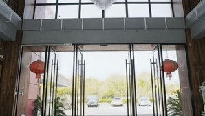 Entrada de hotel com porta de vidro, um candelabro e lanternas vermelhas.