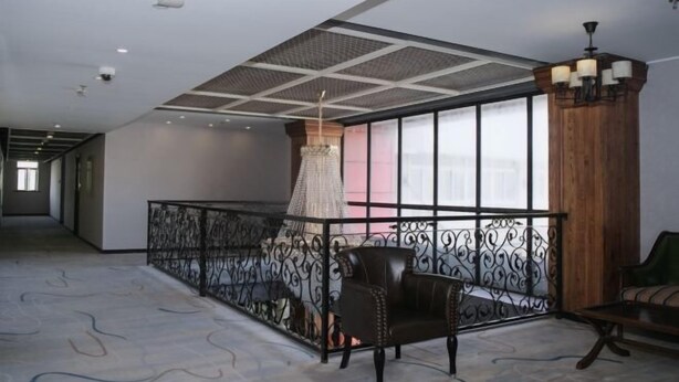 Um hall amplo com teto alto, piso estampado, guarda-corpo decorativo e área de estar com sofá e poltrona.