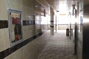 Corredor com paredes revestidas de azulejos, um extintor de incêndio e uma lixeira.
