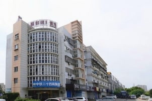 Um edifício de vários andares com fachada curva, placa indicativa de um estabelecimento comercial e estacionamento com carros.