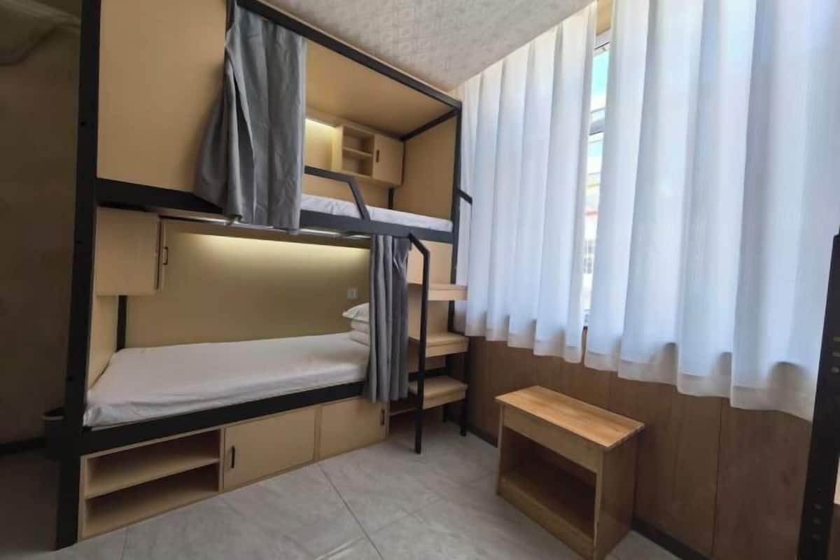 Quarto com beliche, escrivaninha e janela com cortinas.