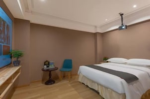 Quarto de hotel com cama, televisão, uma pequena mesa com cadeira e projetor no teto.