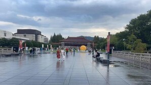 Uma ampla praça ao ar livre, com um edifício tradicional ao fundo, uma grande estrutura esférica amarela e um edifício moderno à esquerda.